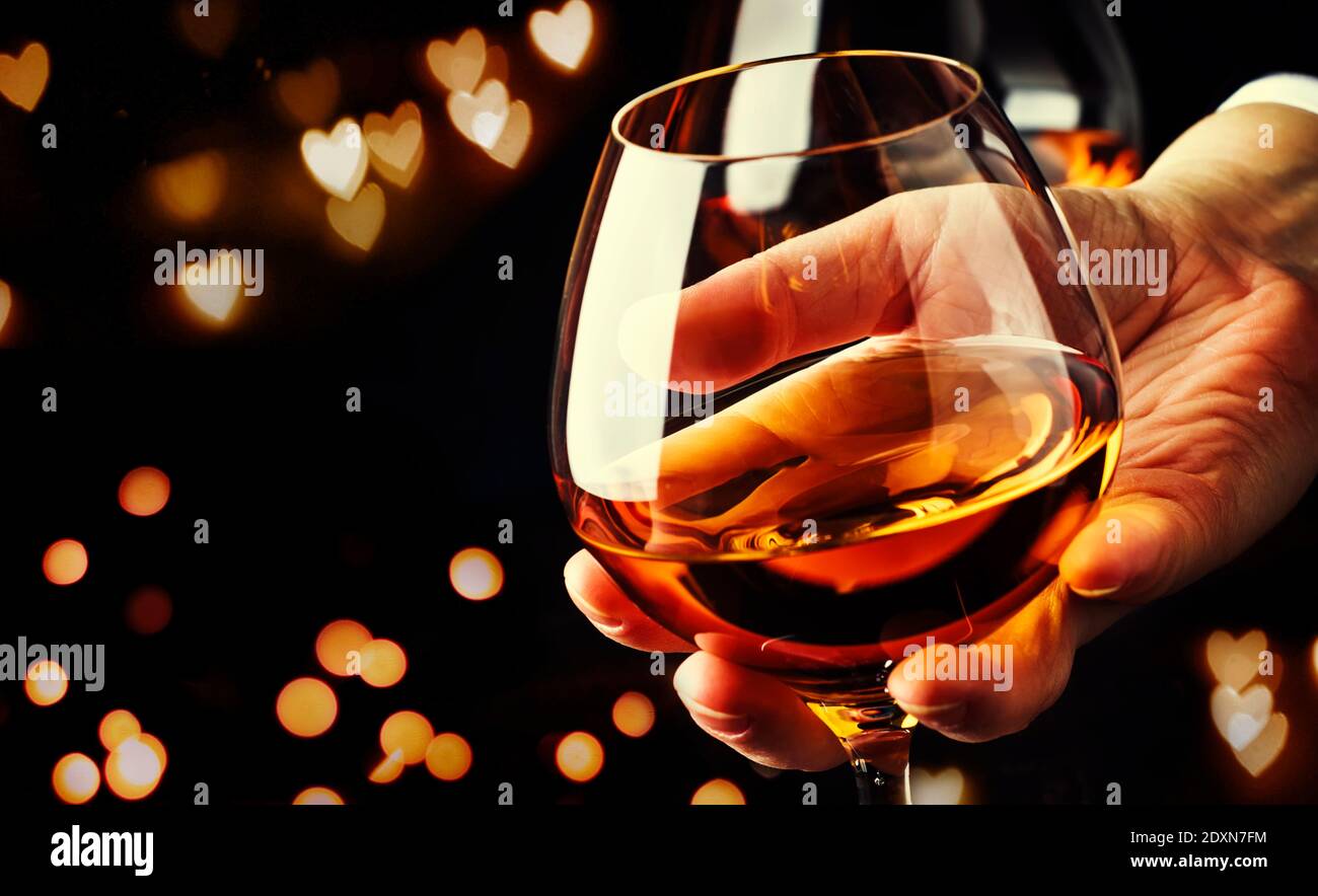 French glowing cognac glass in hand on the dark bar counter background ...