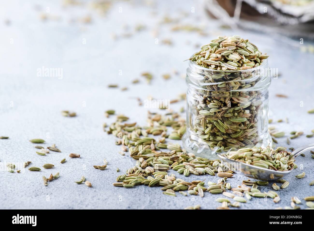 Fennel seeds in a glass jar and a metal spoon, gray kitchen table ...