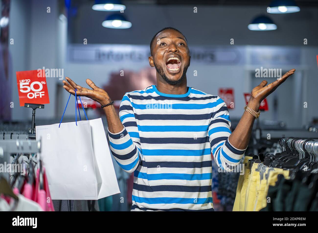 A young African-American excited shopaholic male holding bags with ...