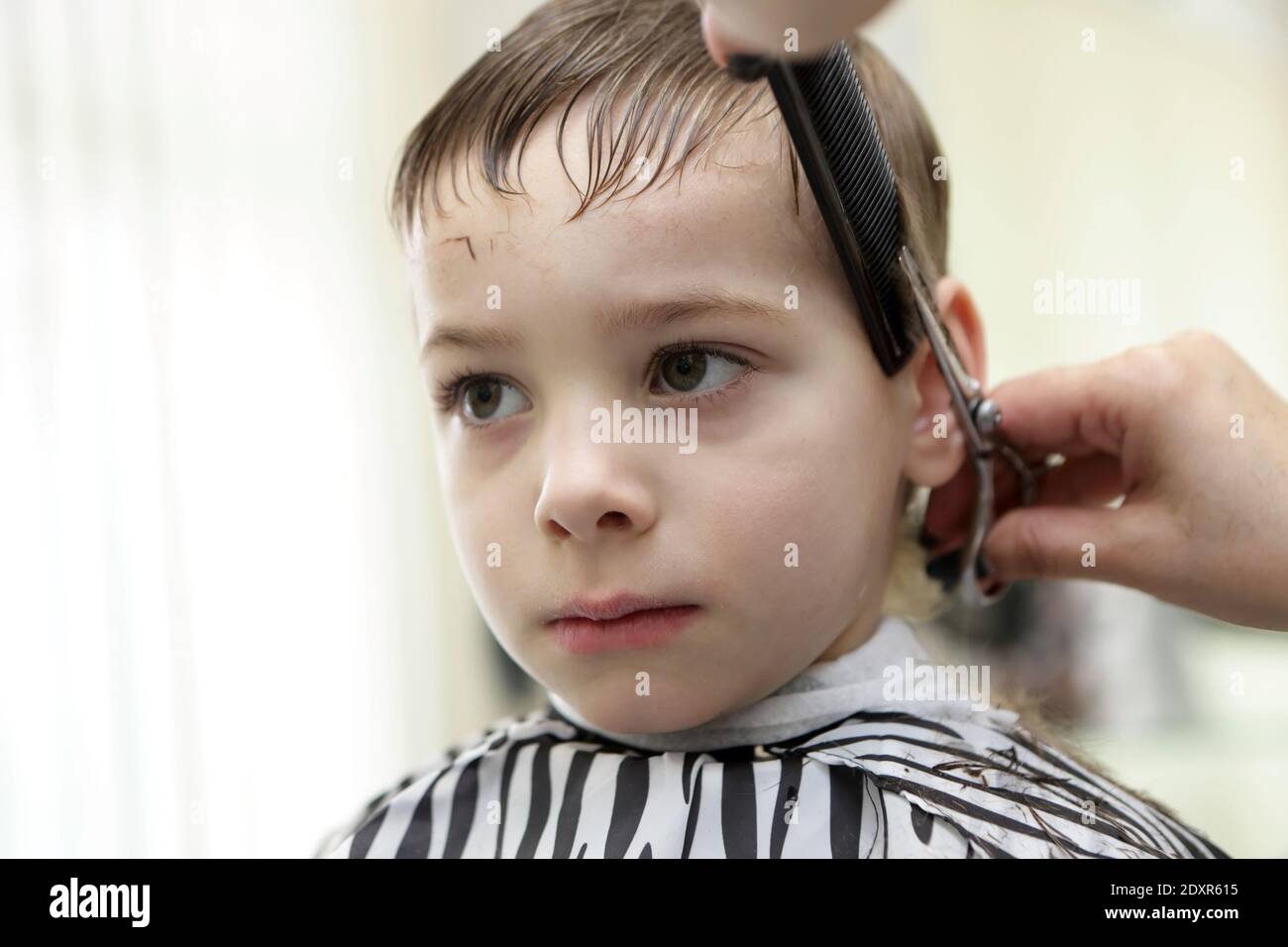Serious child getting haircut at hairdresser salon Stock Photo - Alamy