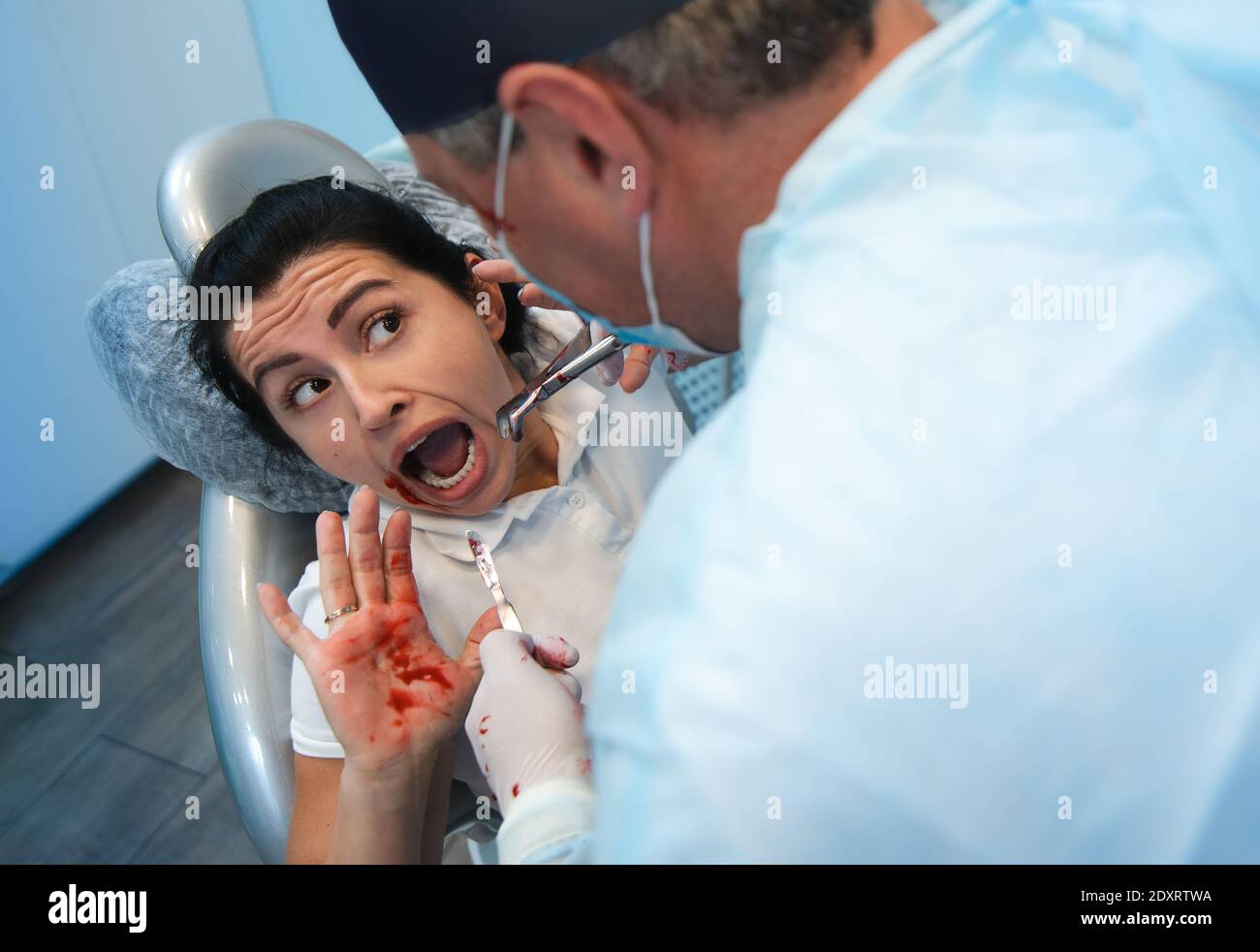 A patient in a dental chair looks scared at a doctor holding blood ...