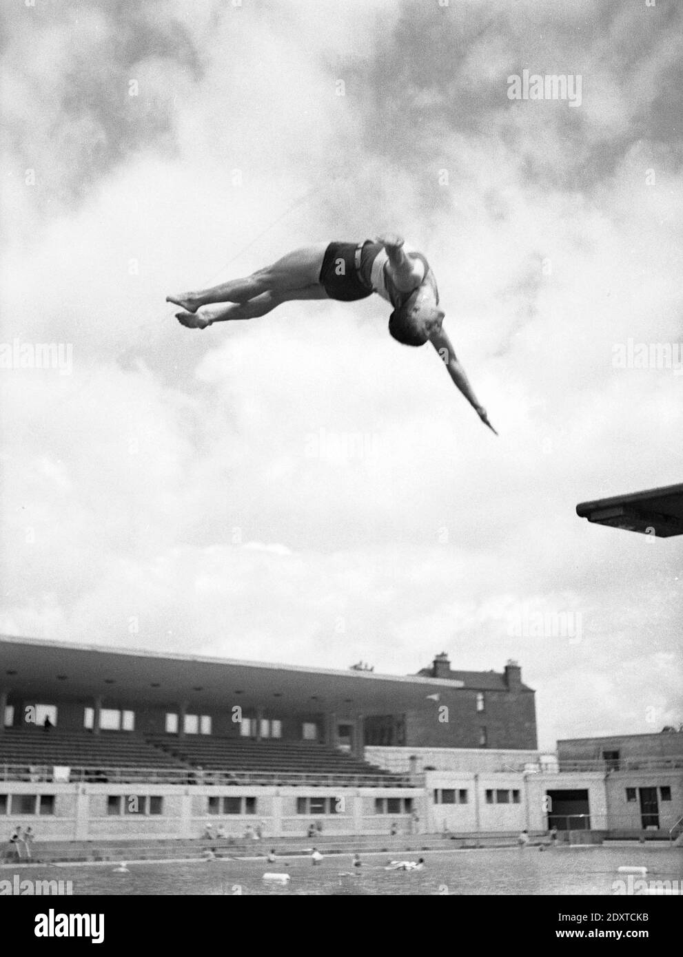 1950s, historical, a male diver doing a twist dive at an open air Lido ...