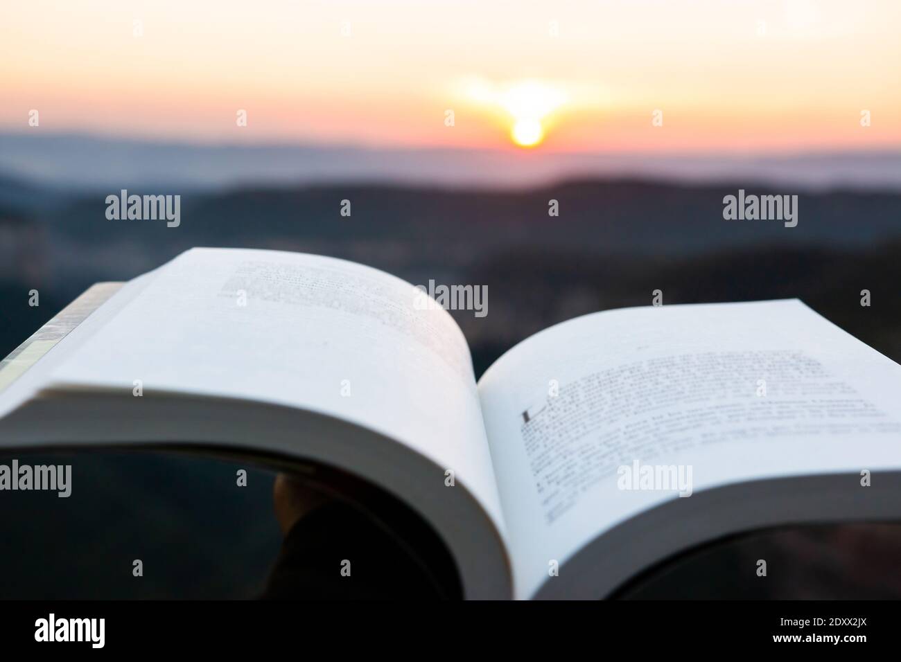 Reading a book in the mountain with sunset or sunrise in the background ...