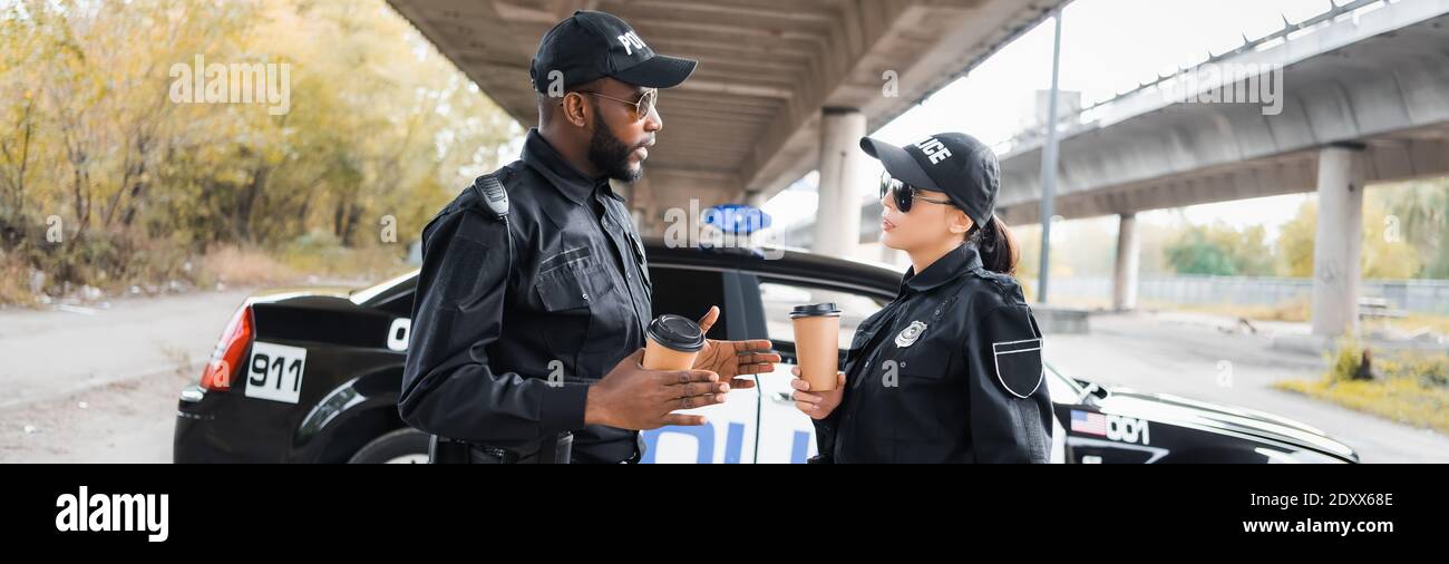 multicultural police officers with paper cups talking near patrol car ...