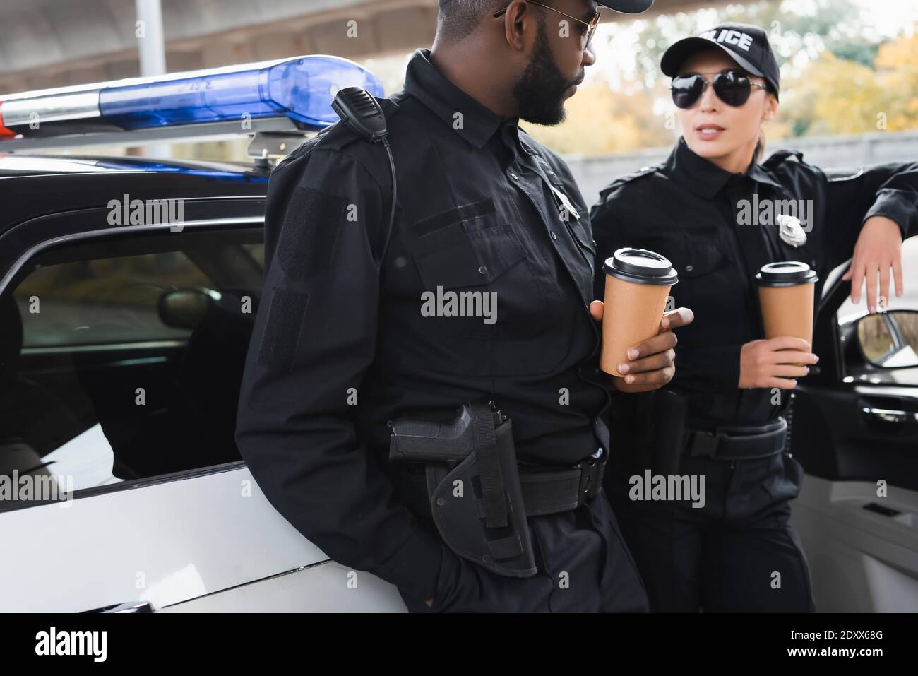 multicultural police officers with paper cups talking while leaning on ...