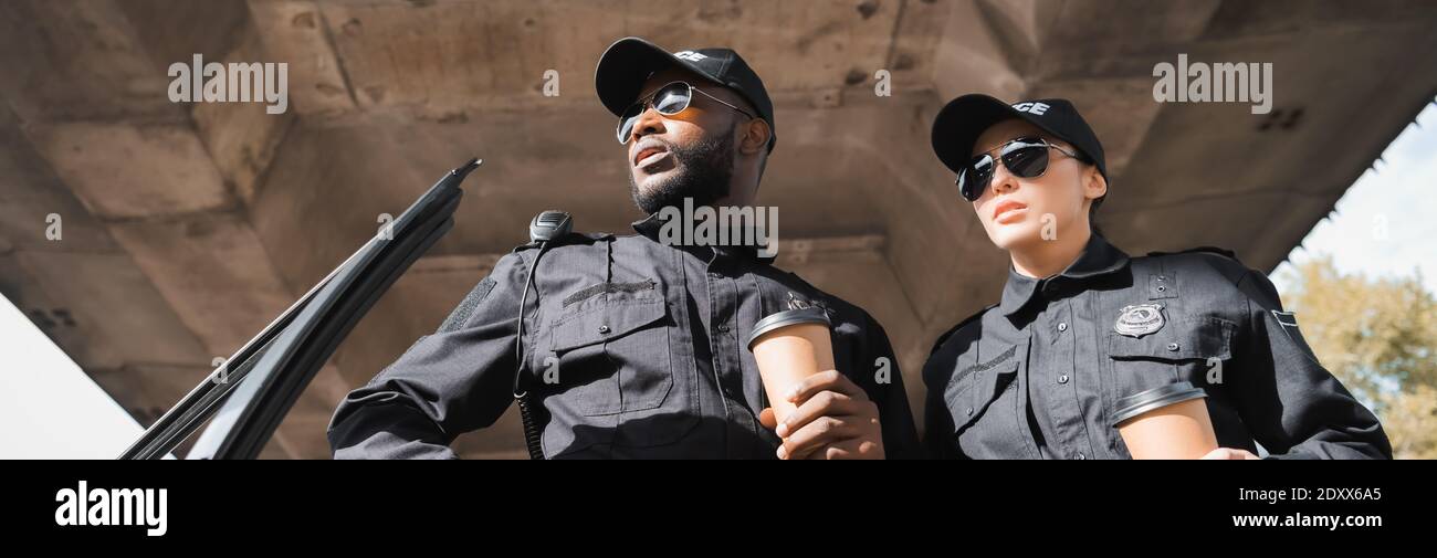 low angle view of multicultural police officers with paper cups looking ...