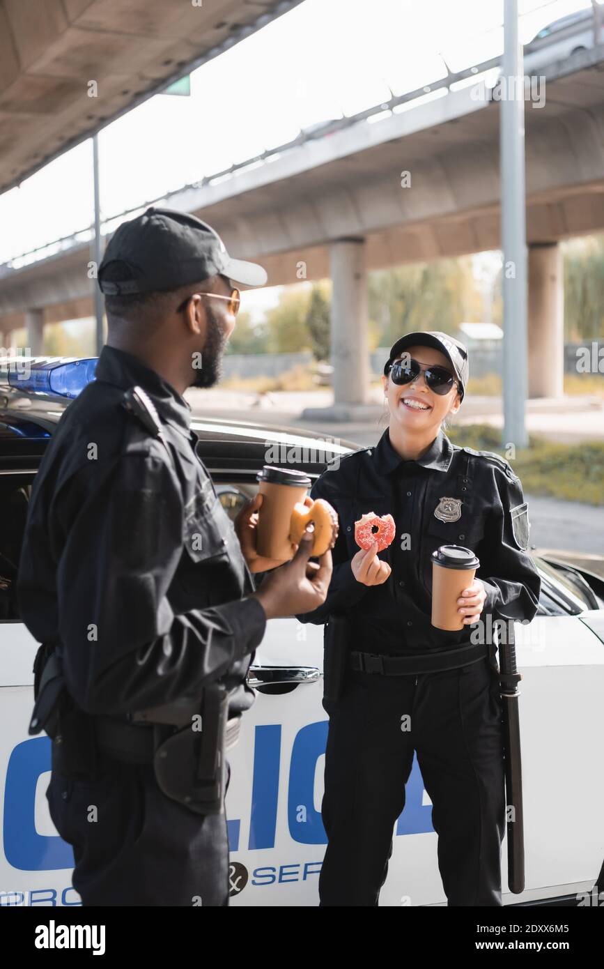 multicultural police officers with paper cups and doughnuts talking ...