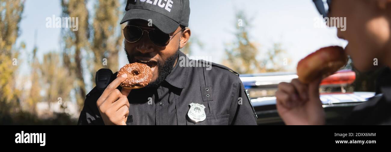 african american police officer eating doughnut with blurred colleague ...