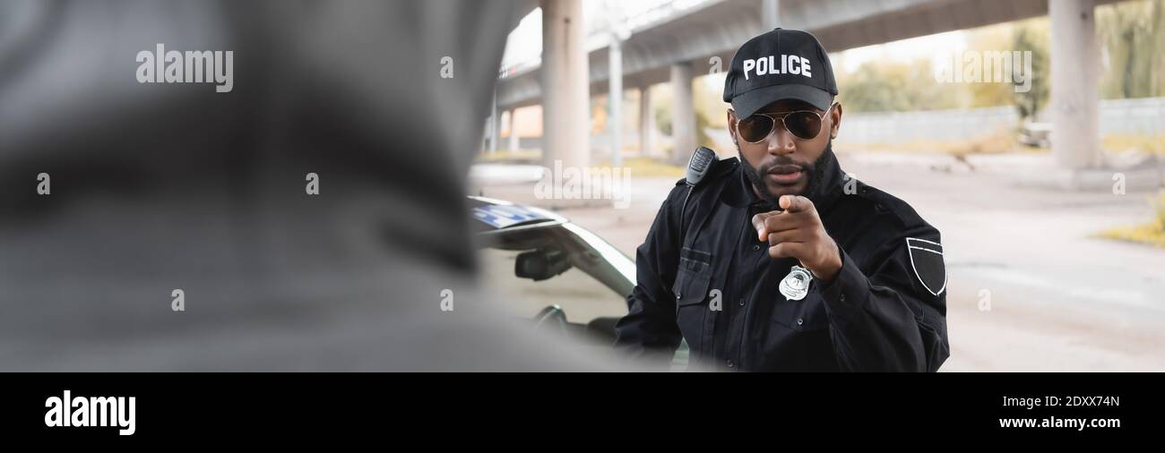 serious african american police officer pointing with finger at blurred ...