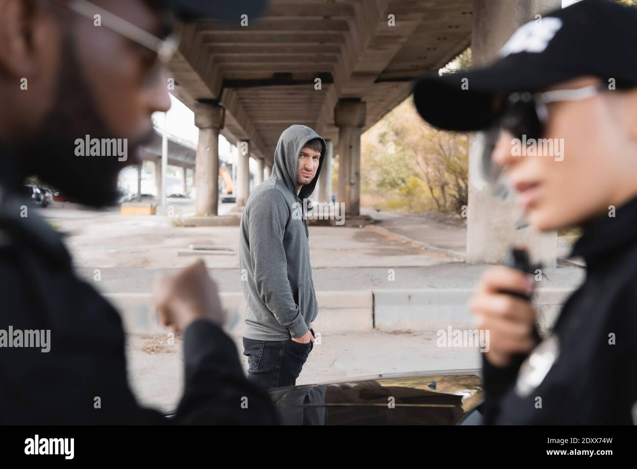 dissatisfied hooded offender looking at blurred multicultural police ...