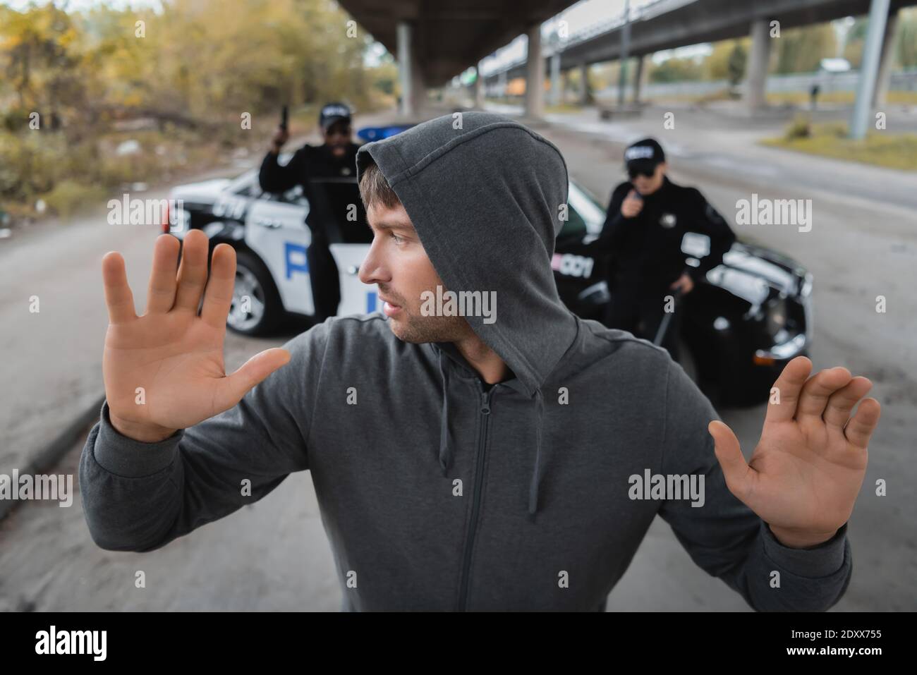 hooded offender with raised hands looking away with blurred ...