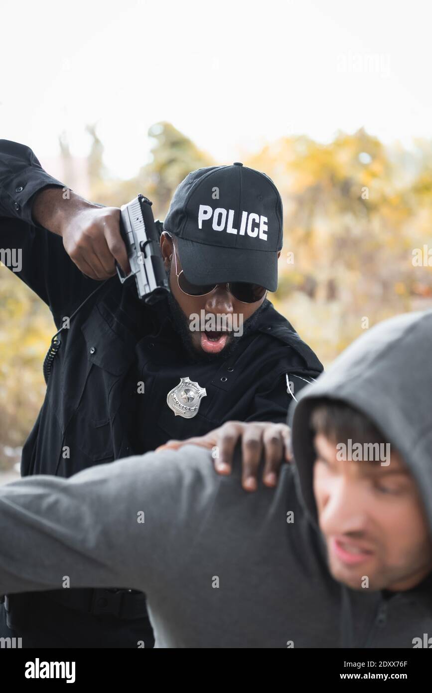 aggressive african american policeman aiming with pistol while ...