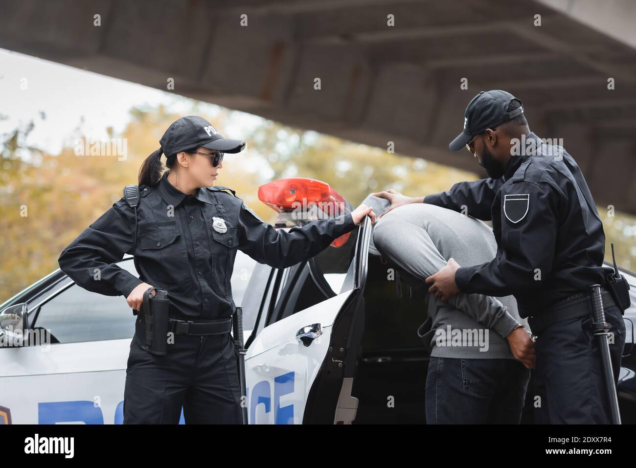 multicultural police officers arresting hooded offender near colleague ...