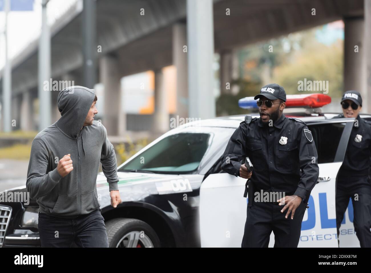 Hooded offender running from multicultural police officers near patrol ...