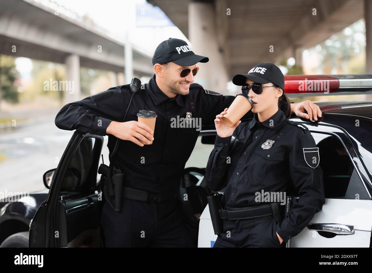 Smiling officer of police in sunglasses looking at colleague drinking ...
