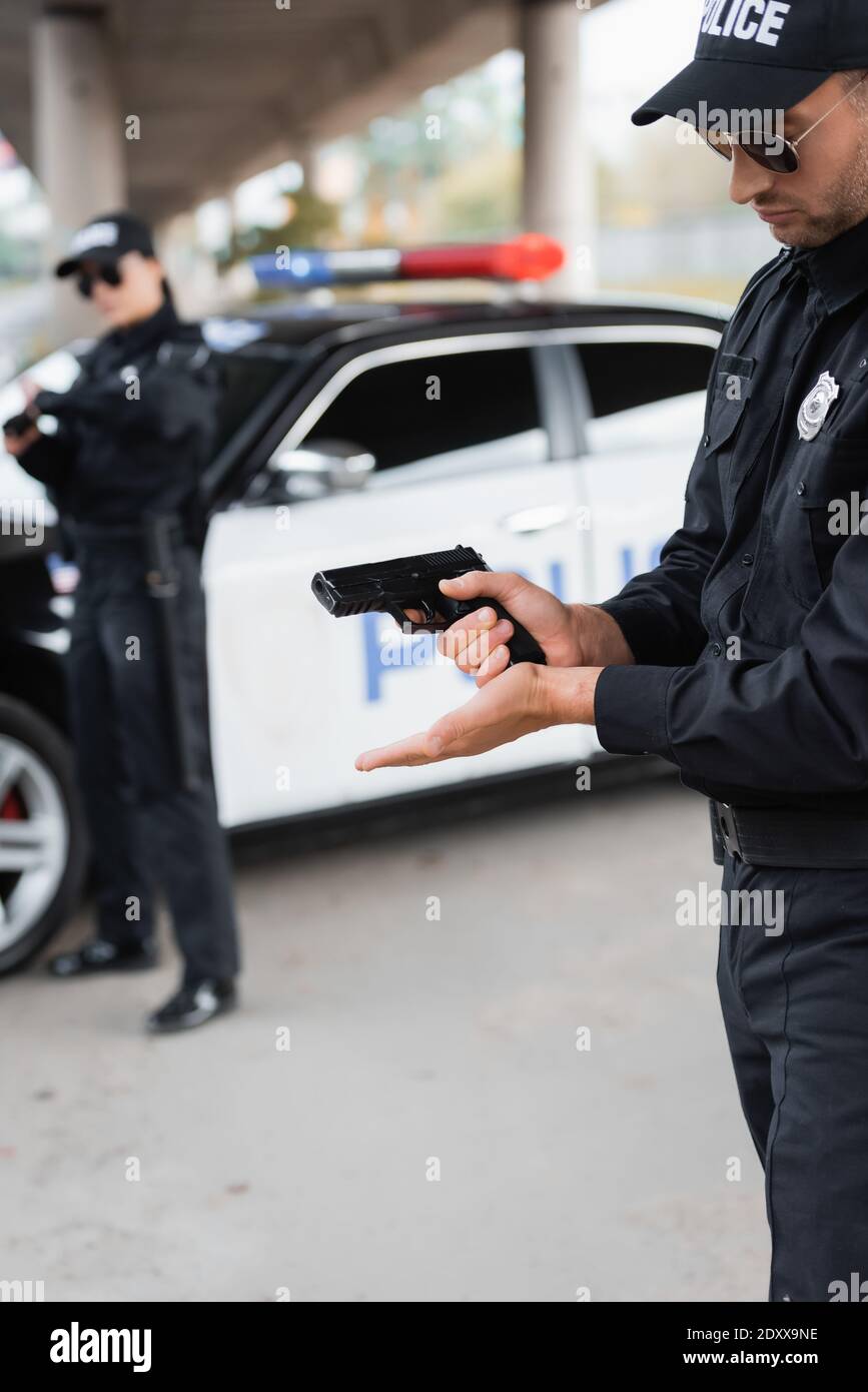 Officer of police loading gun near colleague and car on blurred ...