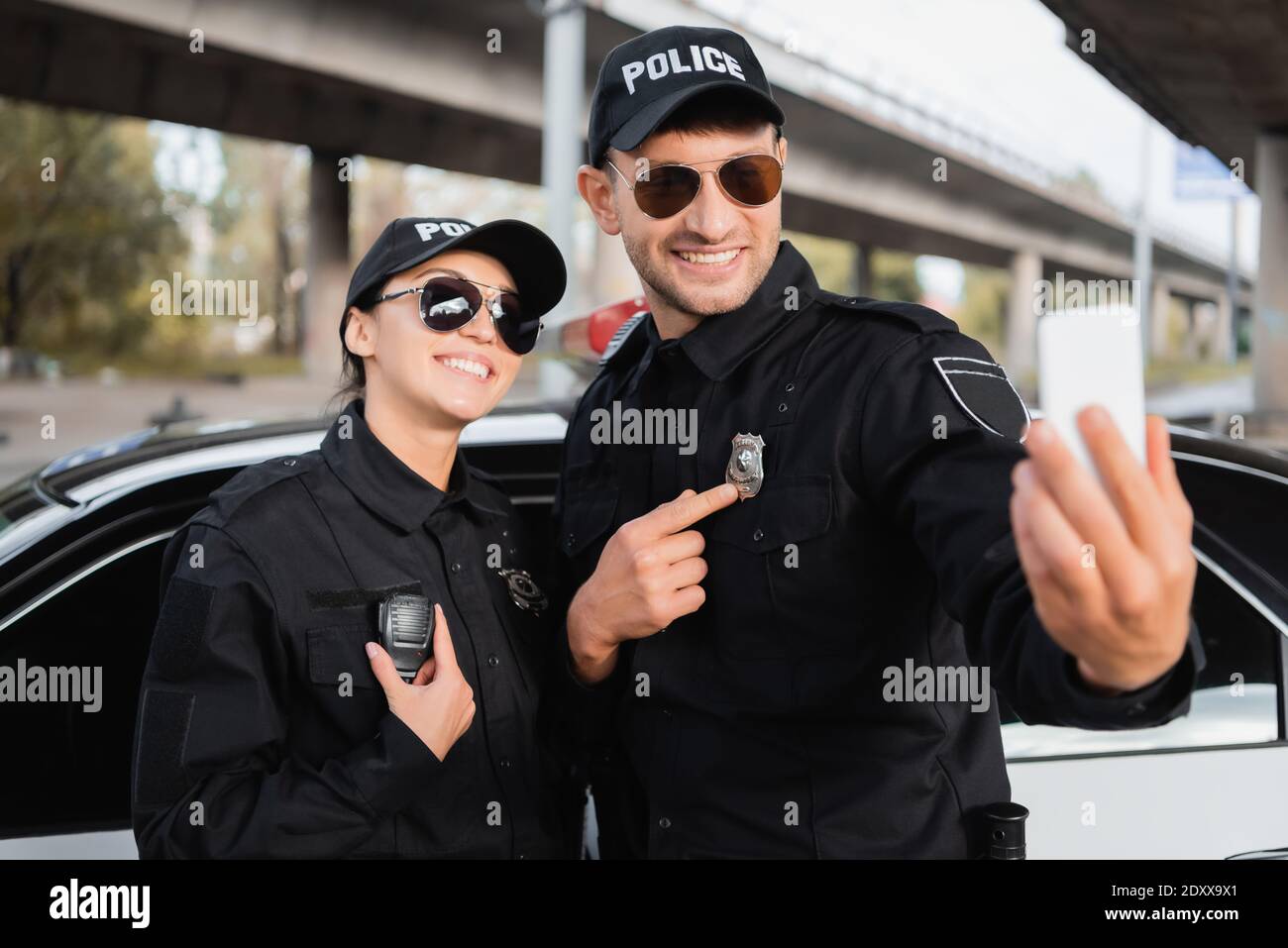 Cheerful police officers showing badge and walkie talkie while taking ...