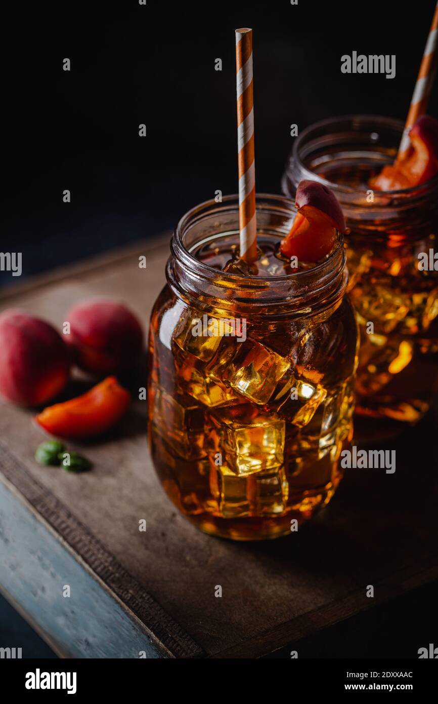 Glass of peach or apricot iced tea with fruit slices against dark blue ...