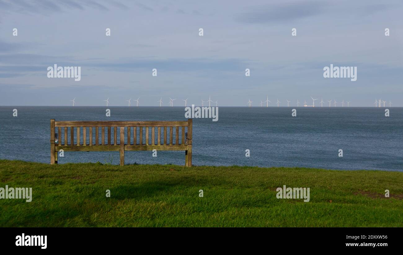 Empty bench on grass facing see with wind farm turbines on horizon ...