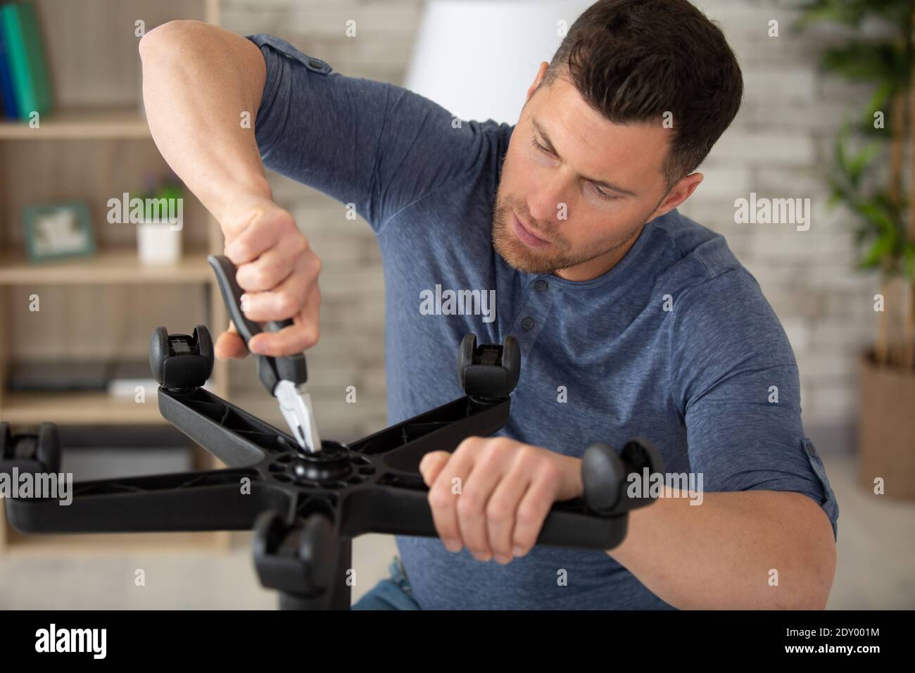 man tightening screw on underside of chair with pliers Stock Photo - Alamy