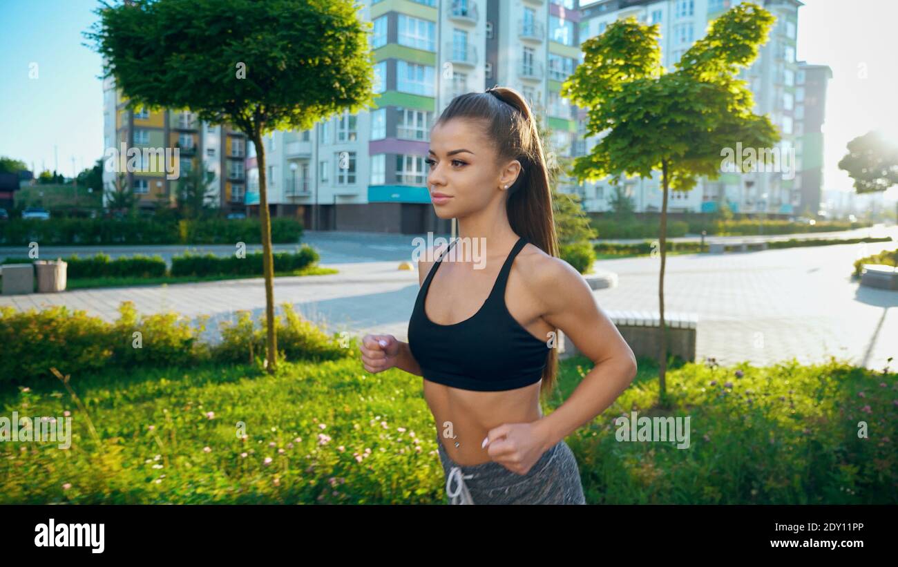 Young gorgeous female runner with perfect body jogging in sunny summer ...