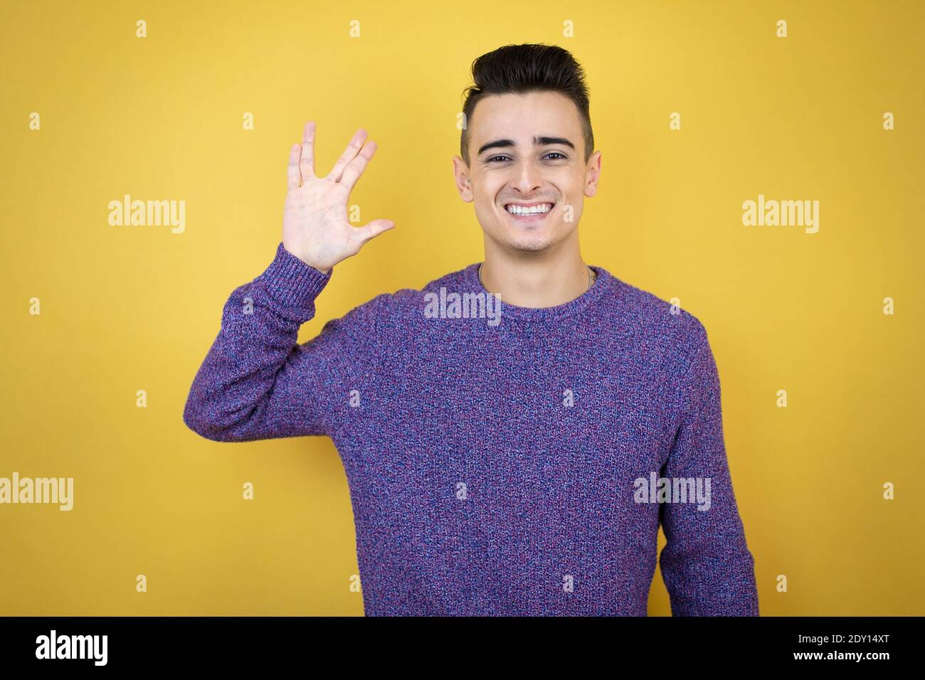 Young caucasian man over isolated yellow background doing star trek ...
