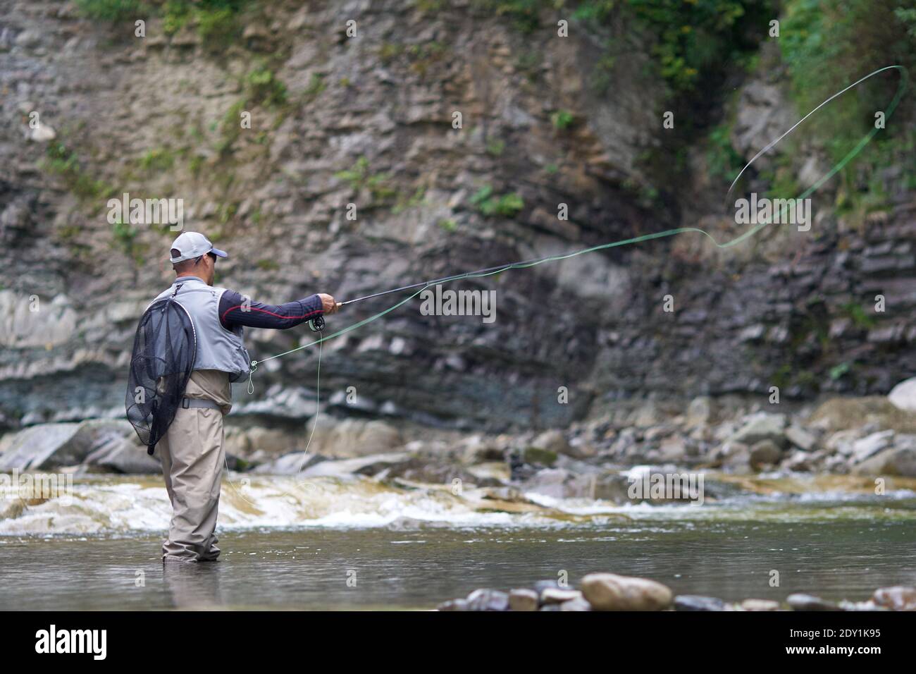 Professional fisherman in waterproof outfit throwing rod into rough ...