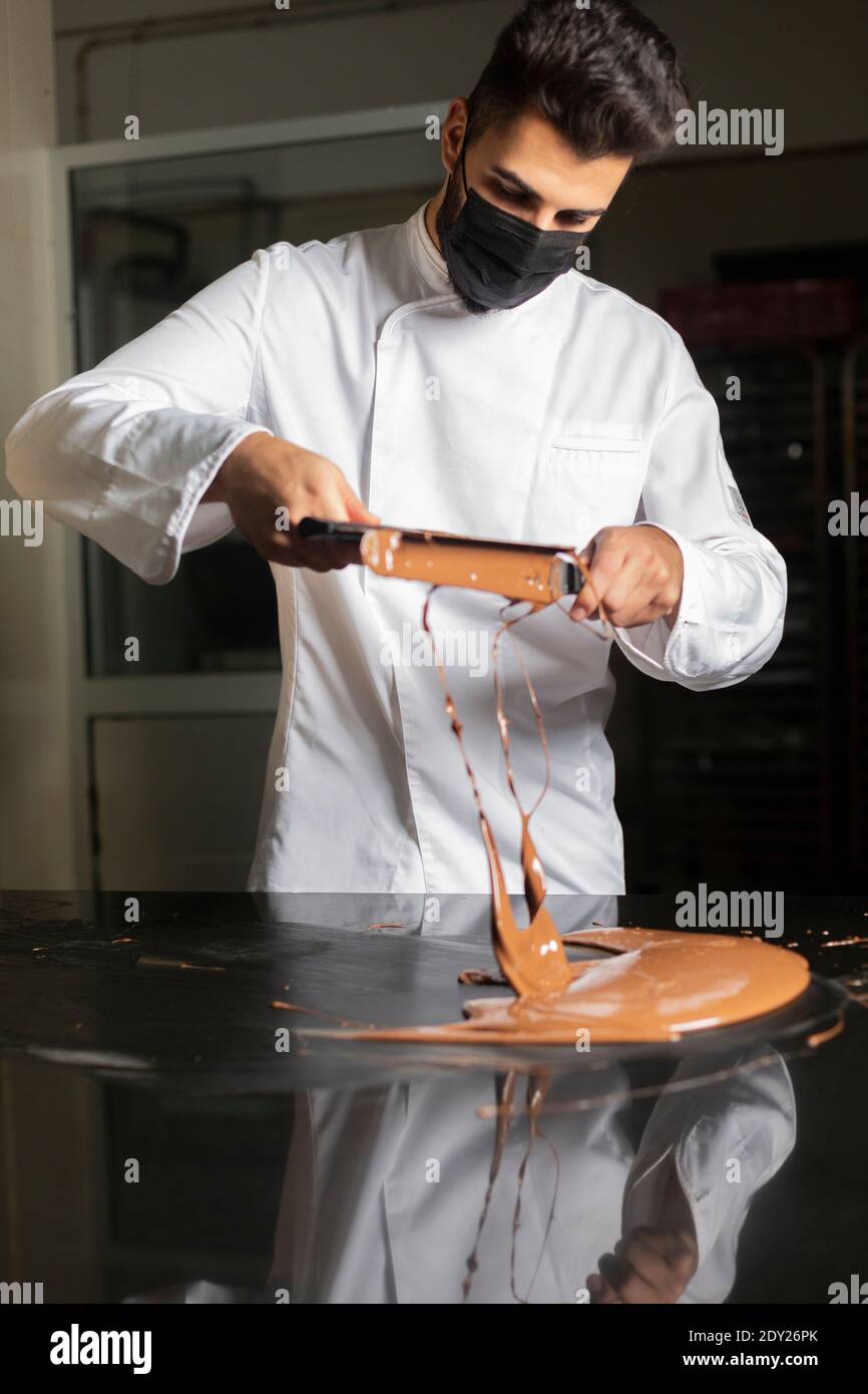 Young pastry chef with mask working on tempering chocolate Stock Photo ...