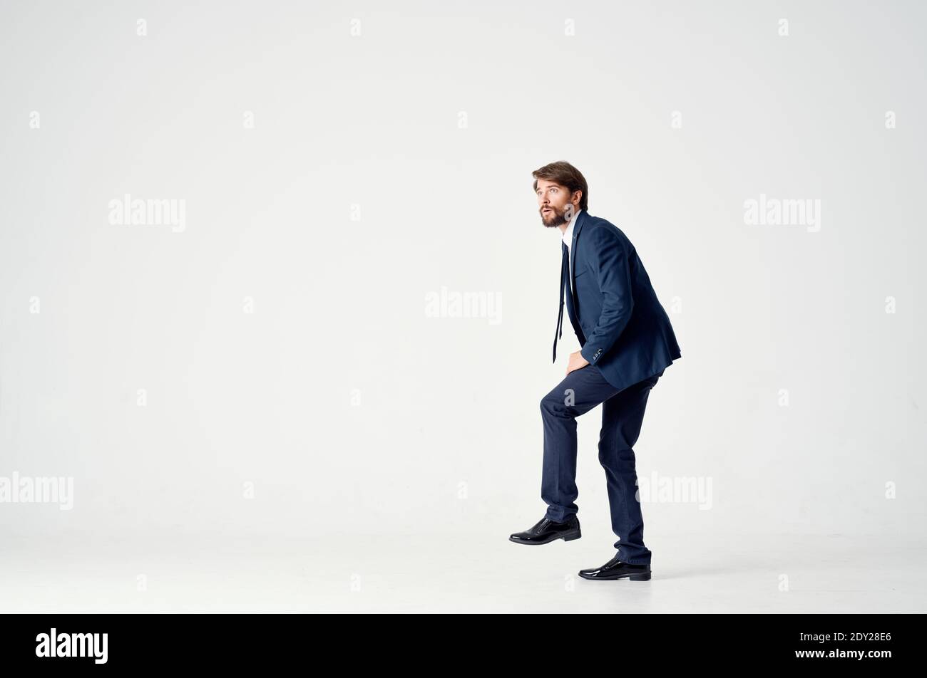 business man in a blue suit stands on one leg on a light background ...