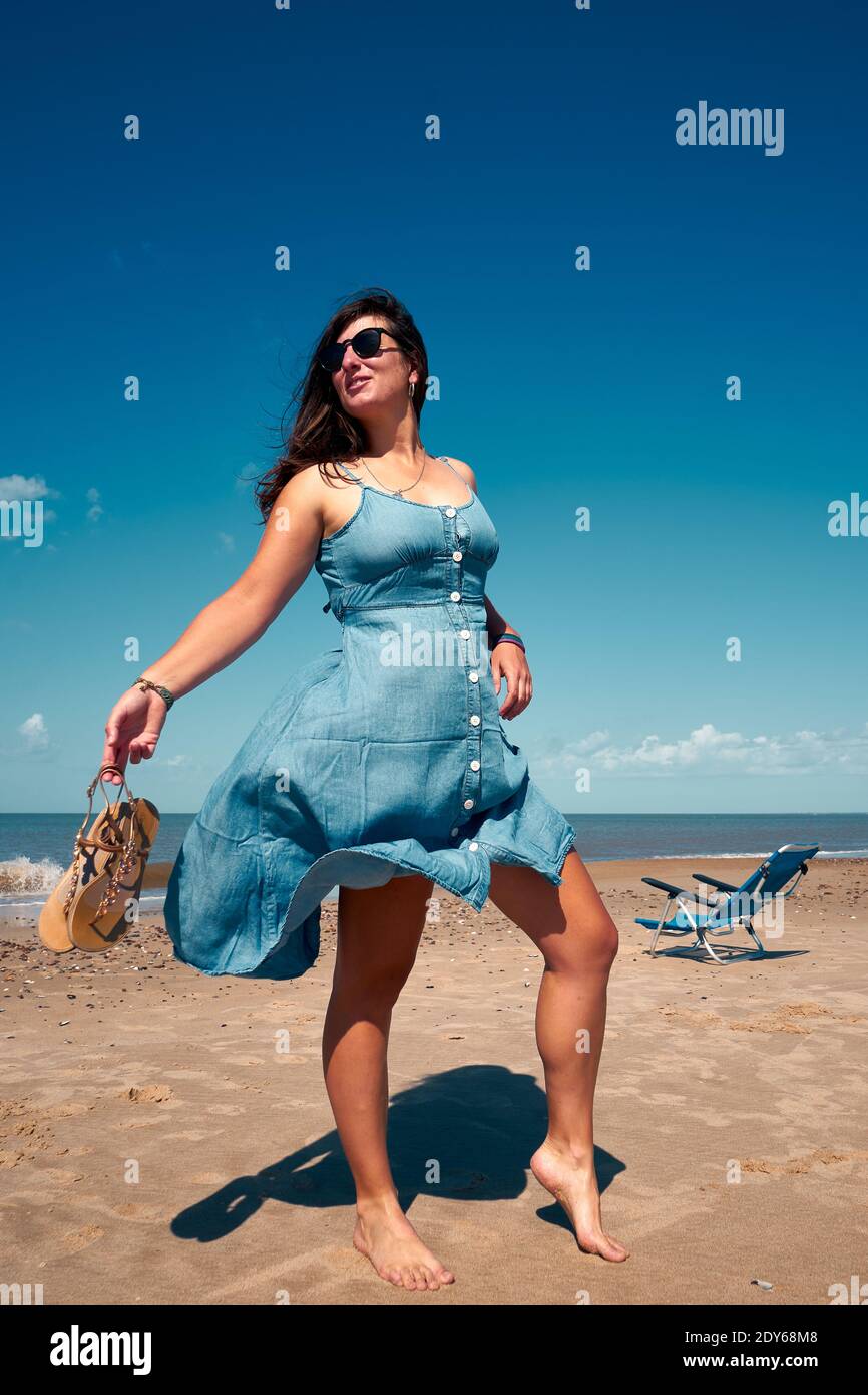 A vertical shot of a young barefoot female in a blue summer dress ...