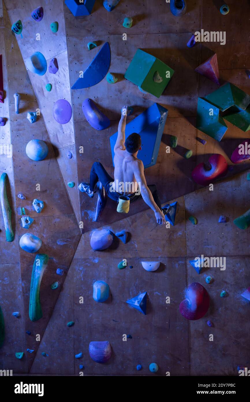 Back view of strong guy hanging on grips of climbing wall during ...