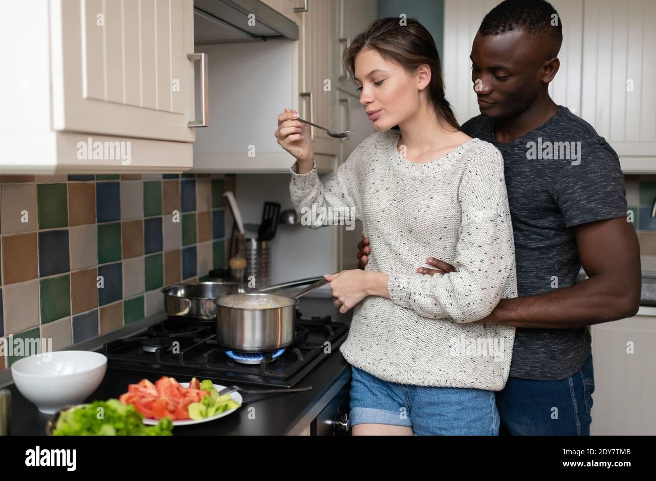 Black guy hugging young girlfriend from back while trying boiling ...