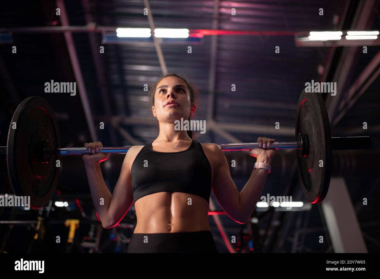 From below concentrated slim lady with barbell on shoulders exercising ...
