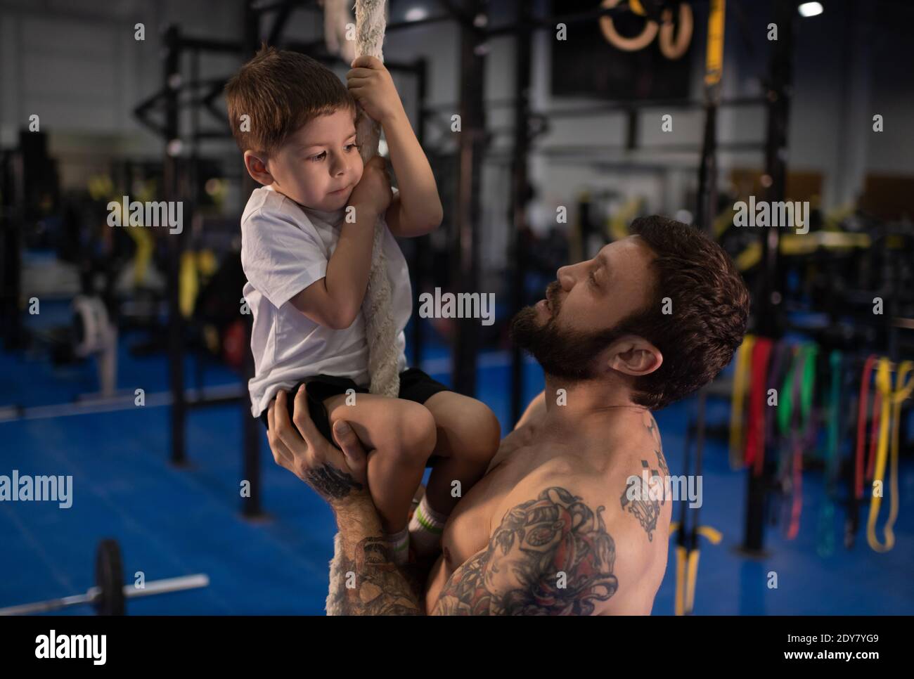 Side view of muscular tattooed man pushing determined boy climbing rope ...