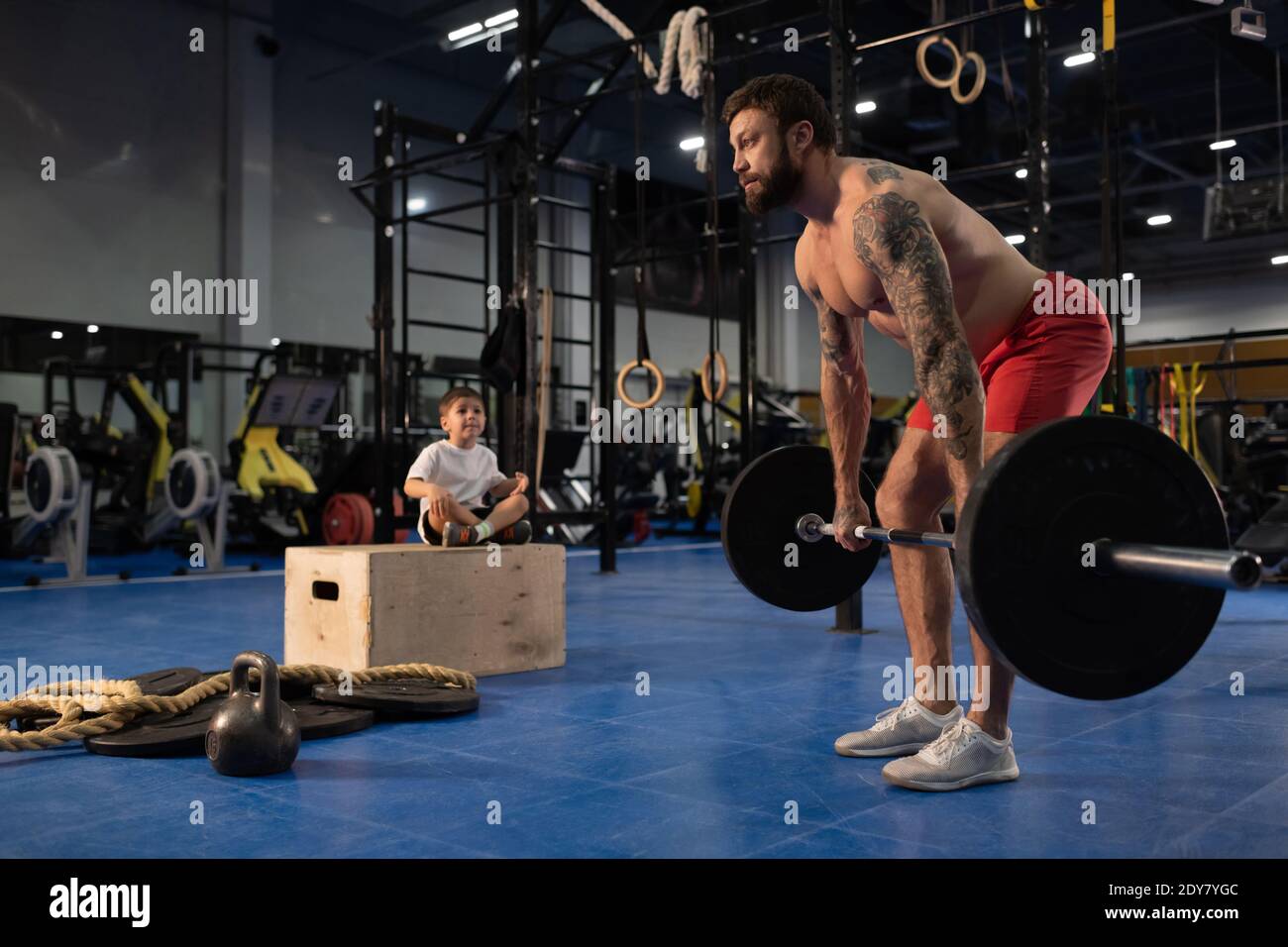 Little boy sitting on box and watching muscular sportsman deadlifting ...