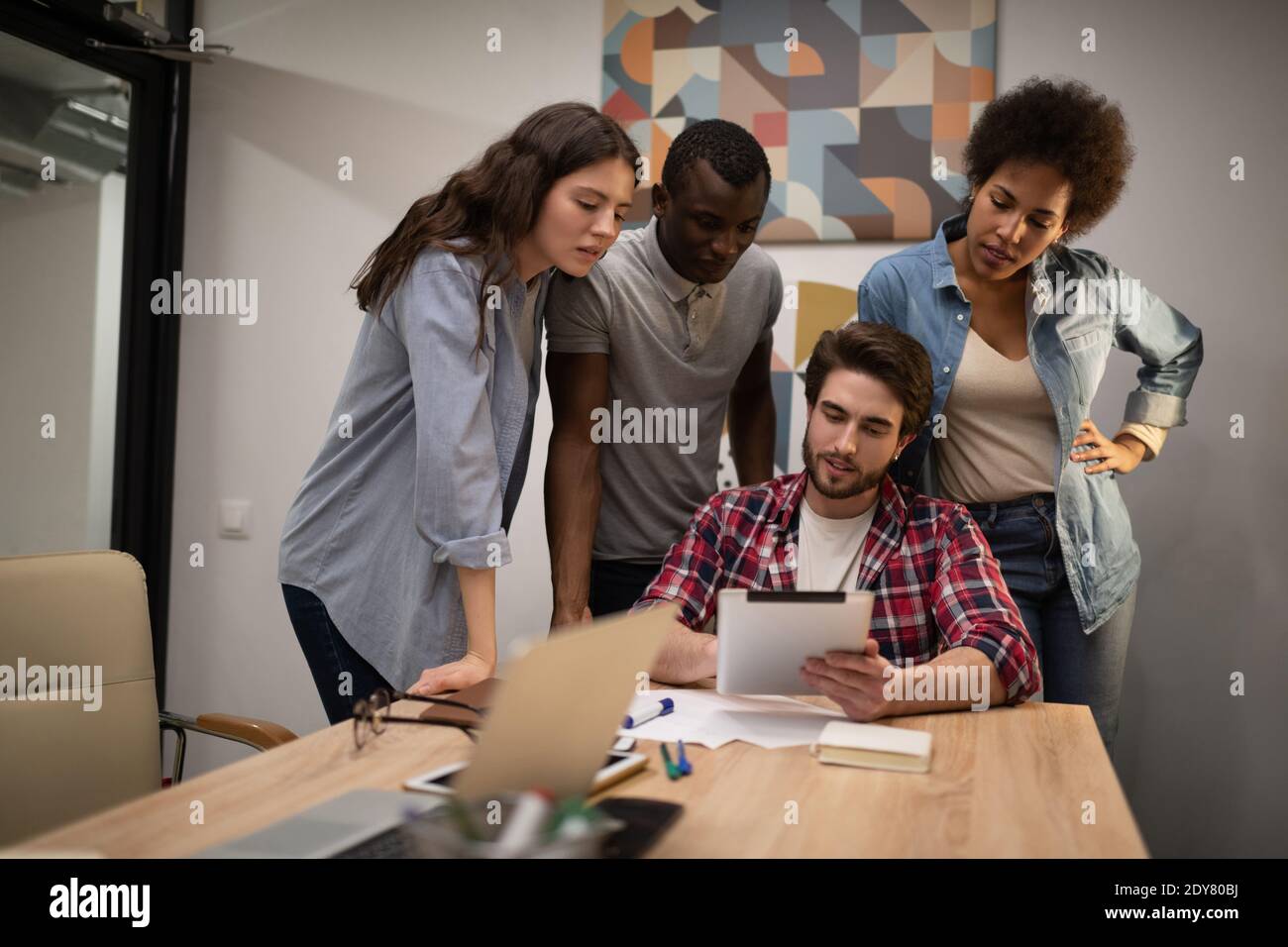 Group of multiethnic colleagues gathering around man with tablet and ...