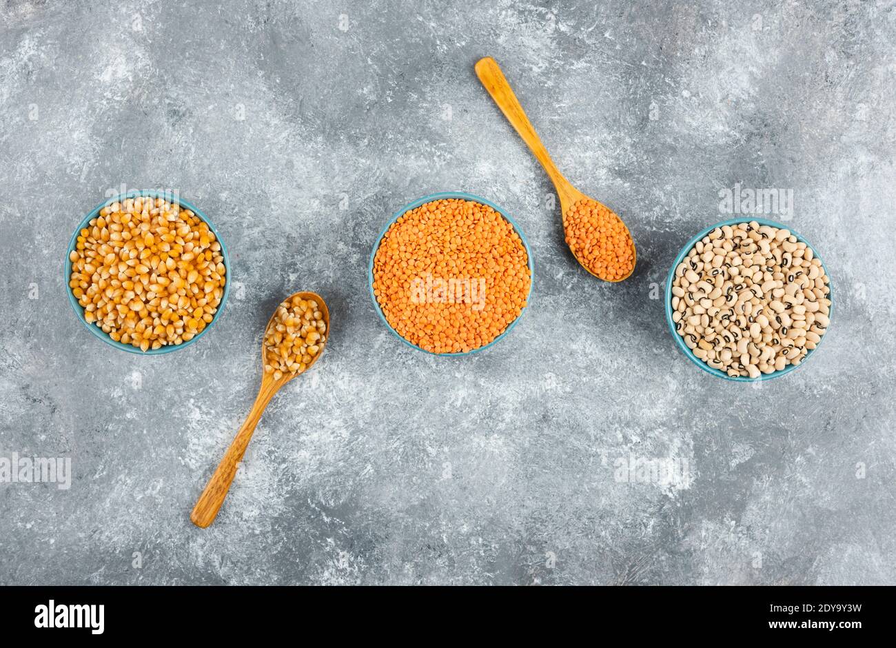 Three bowls of corn kernels, beans and red lentil on marble surface ...