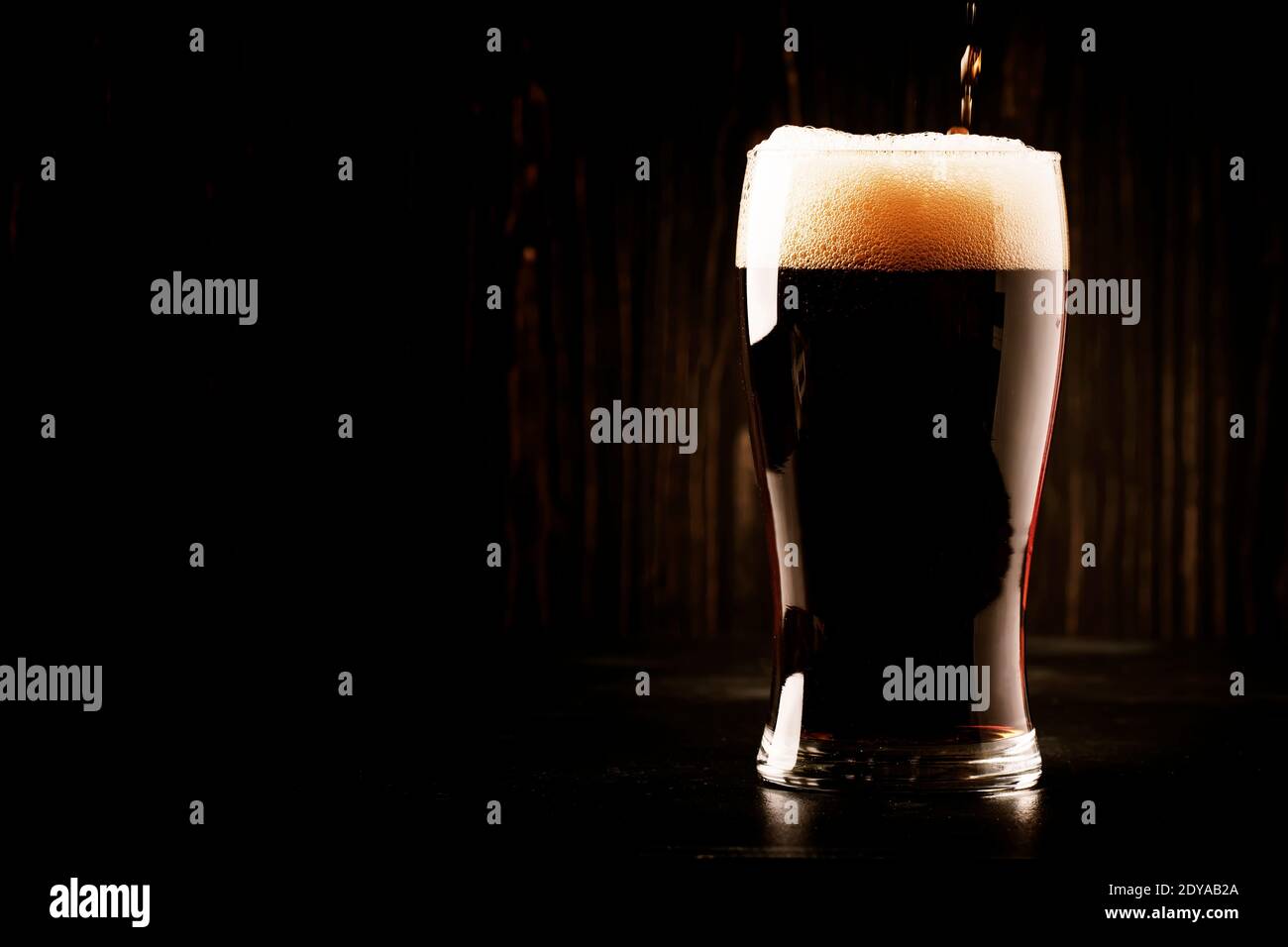 Dark english beer, ale or stout is poured into glass, dark bar counter ...