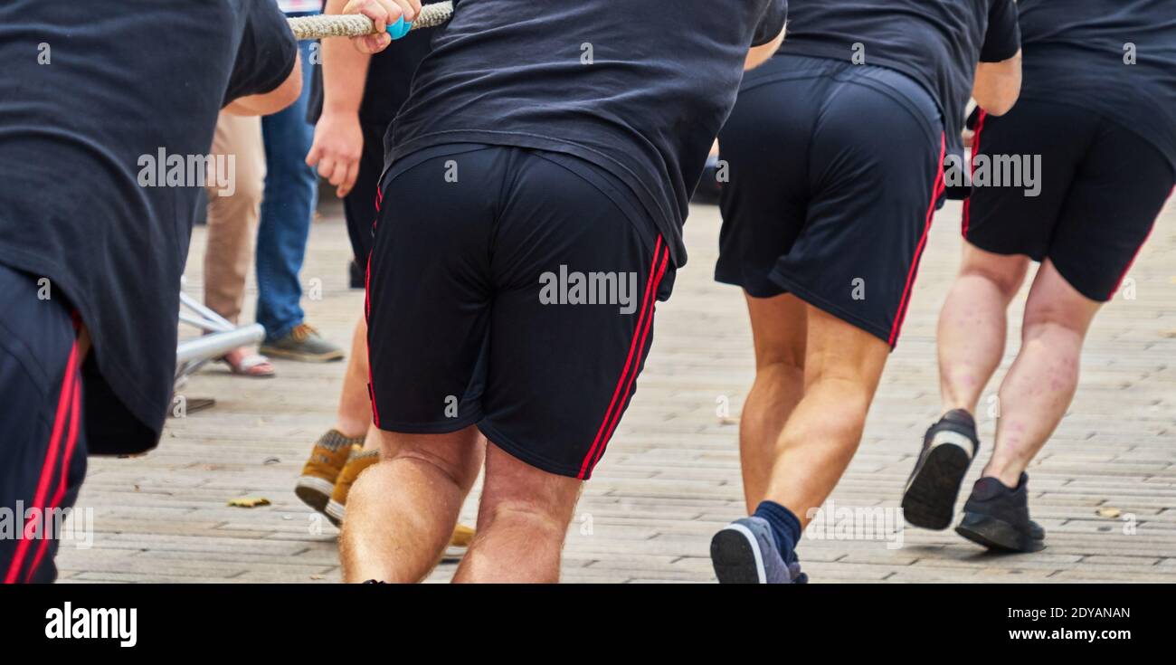 Fat sportsmen in short black pants with red stripes pull together on a ...
