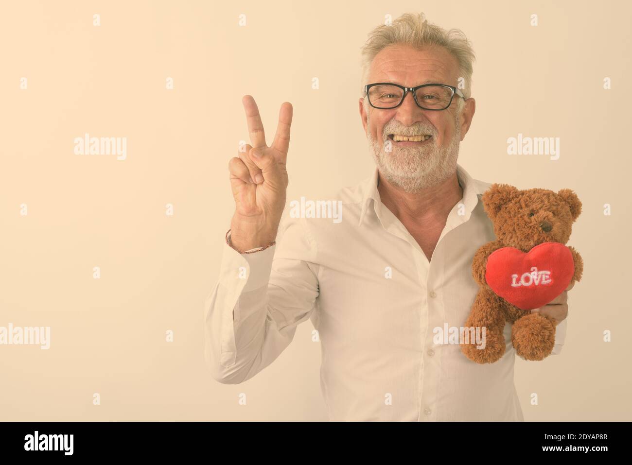 Studio shot of happy senior bearded man smiling and giving peace sign ...
