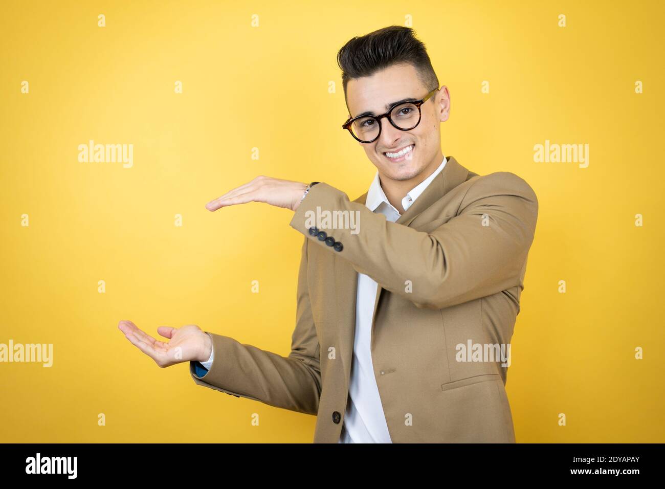 Young business man over isolated yellow background gesturing with hands ...