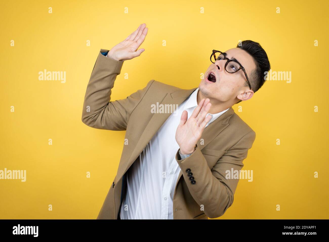 Young business man over isolated yellow background scared with her arms ...