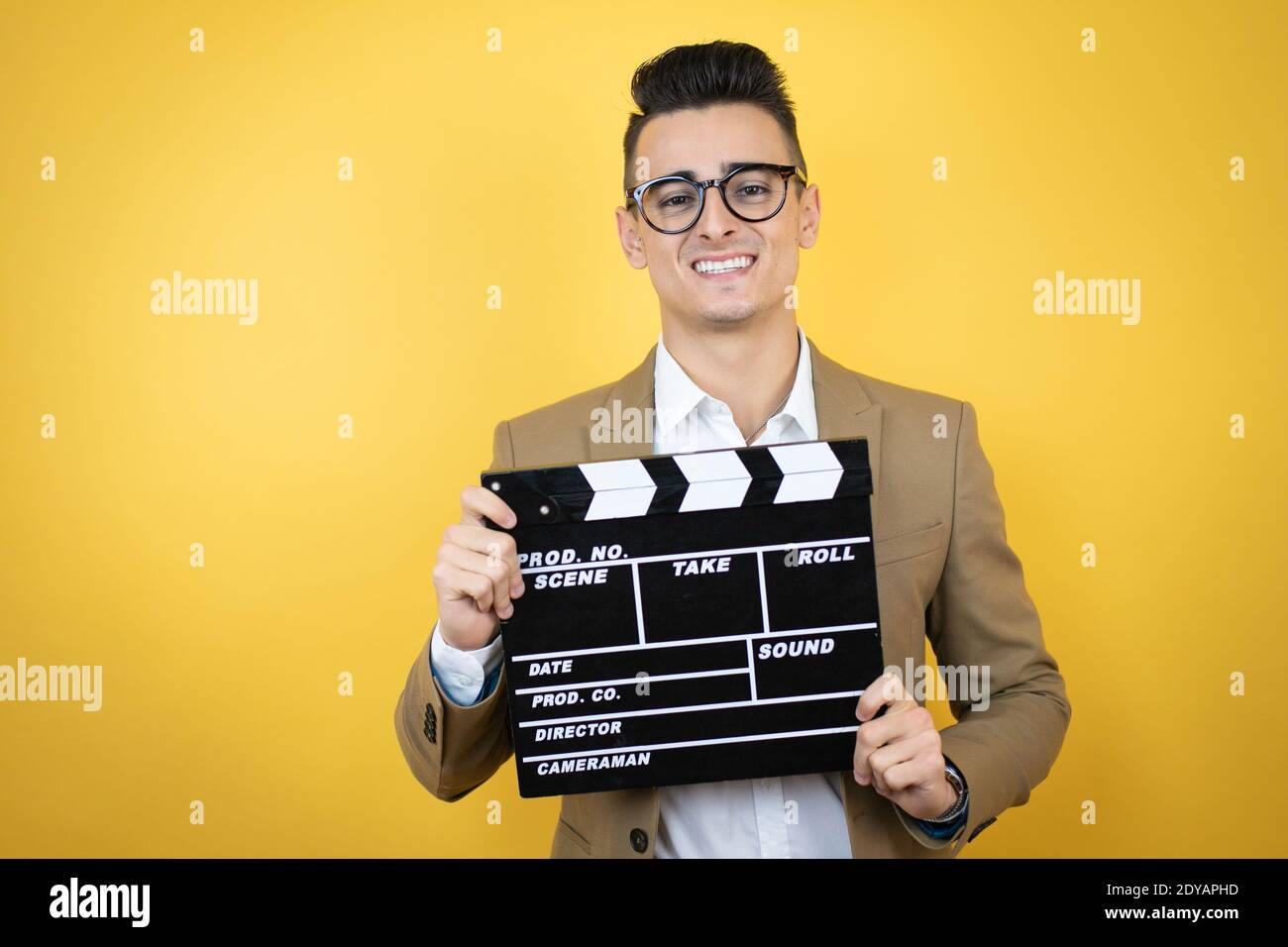 Young business man over isolated yellow background holding clapperboard ...