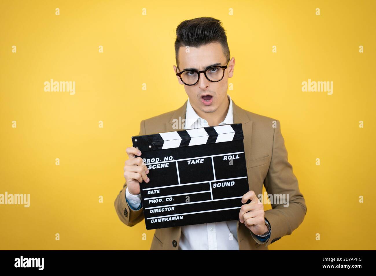 Young business man over isolated yellow background holding clapperboard ...