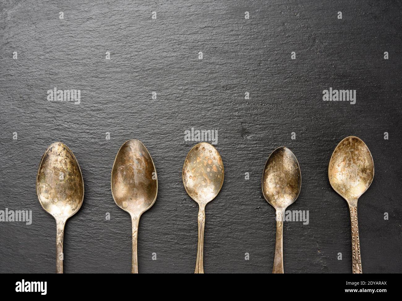 vintage metal empty spoons on black graphite background, top view, copy ...