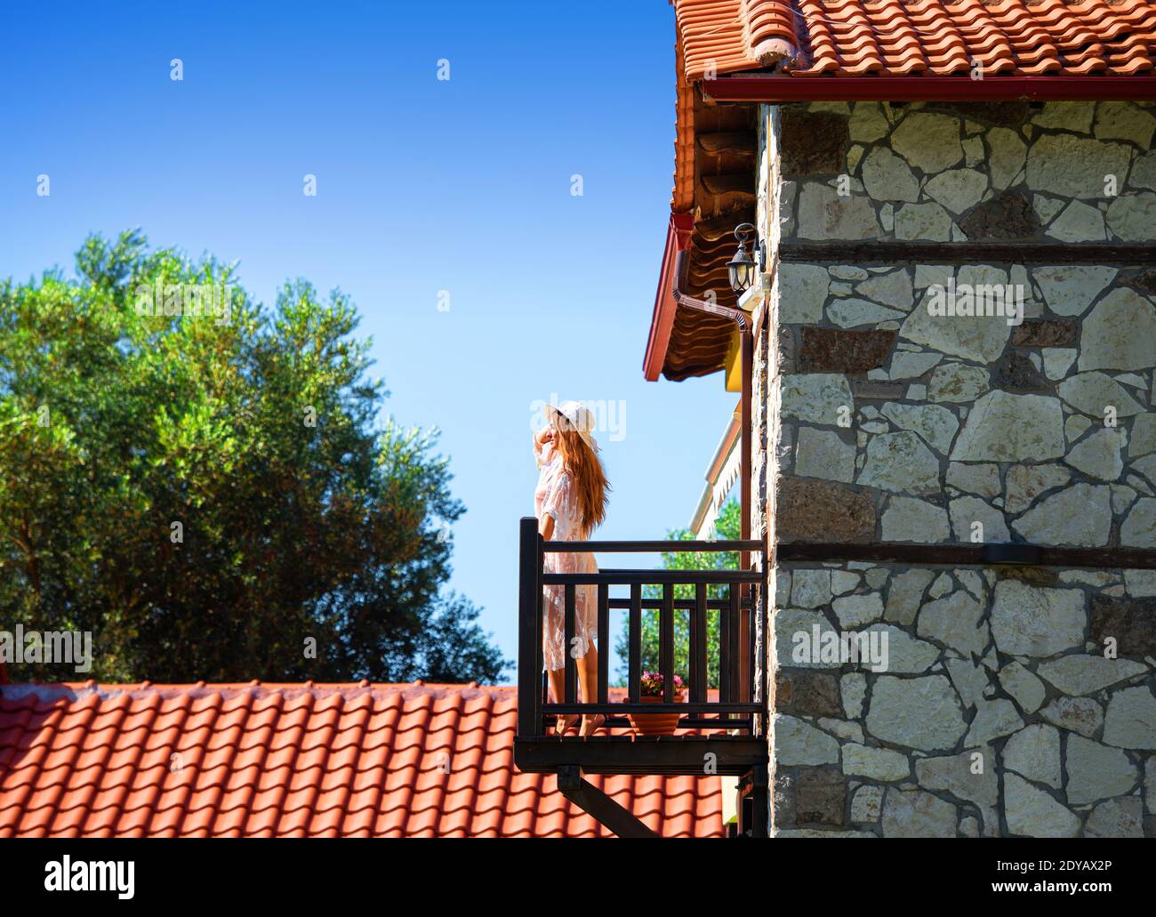 Side view of young woman standing on wooden balcony of old cobble stone ...