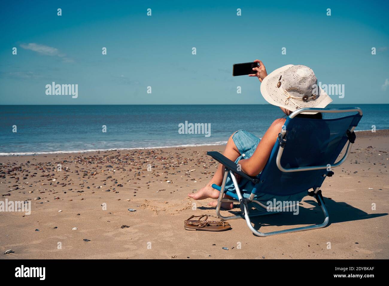 A backshot of a female in a Panama hat sitting in sunbed and taking ...