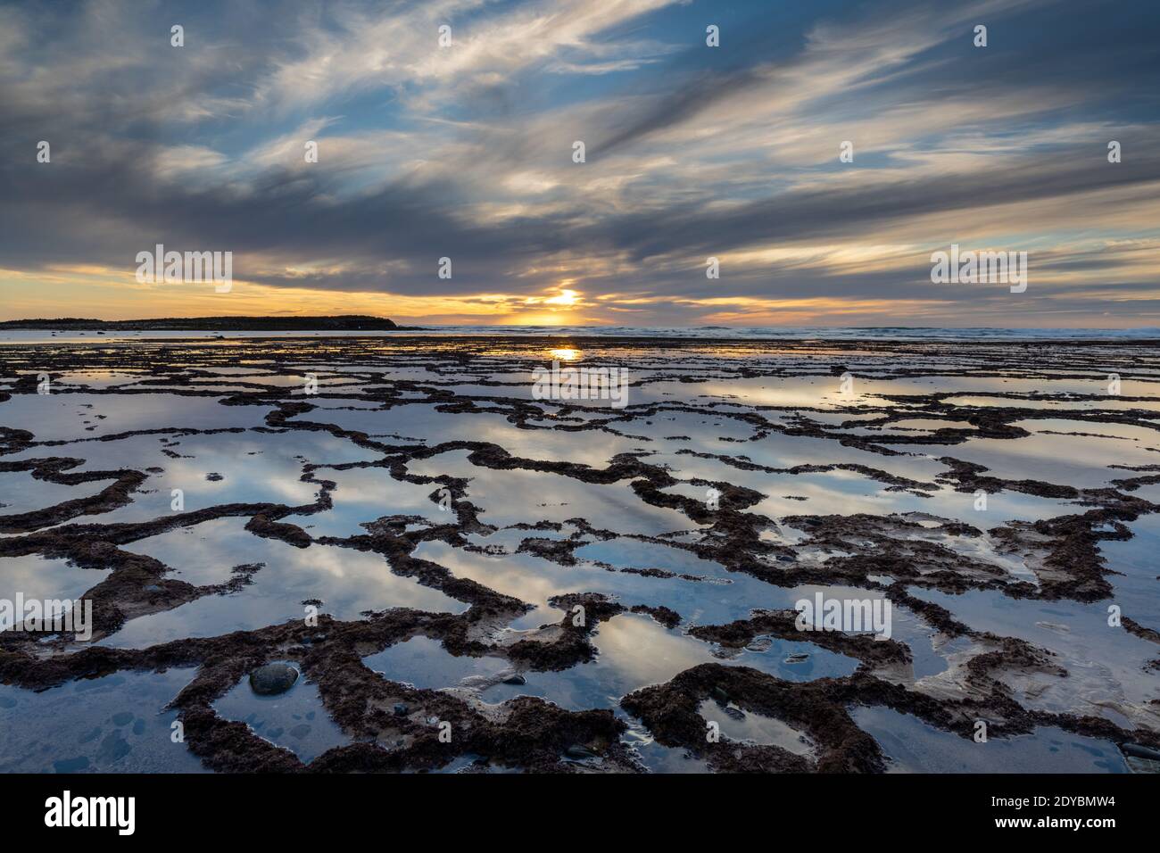 A beautiful sunset over the ocean with rocky beach and tidal pools in ...