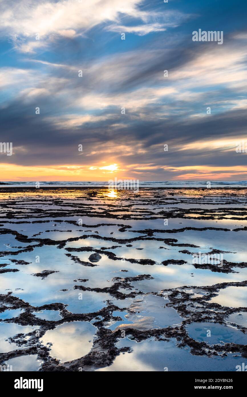 A vertical view of a beautiful sunset over the ocean with rocky beach ...