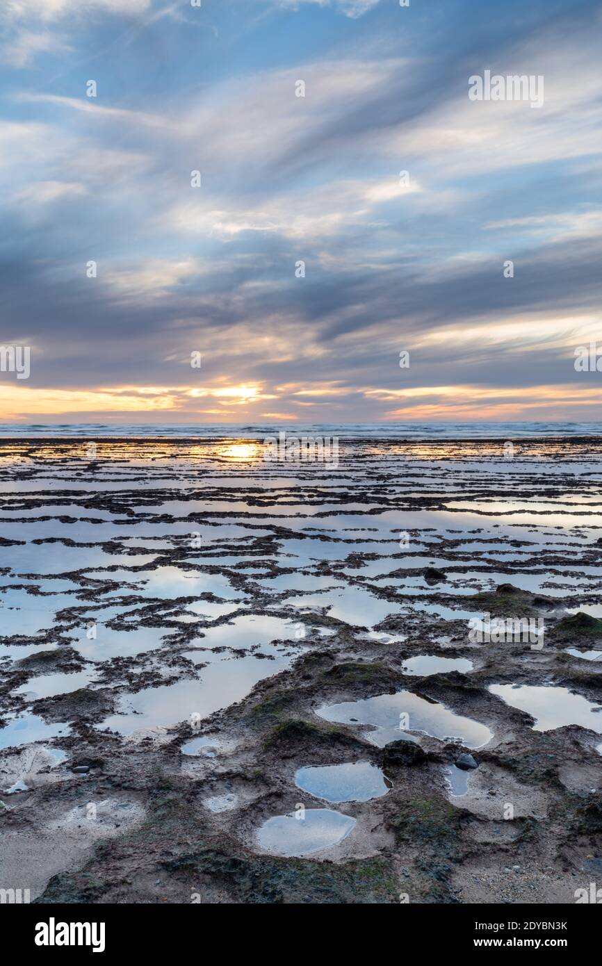 A vertical view of a beautiful sunset over the ocean with rocky beach ...